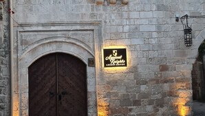 Um edifício de pedra com uma grande porta de madeira, várias janelas com persianas e uma placa com o nome e o número do estabelecimento.