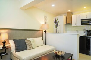 Um espaço compacto para relaxar, com sofá, mesa pequena, luminária, área de cozinha equipada com micro-ondas e geladeira.