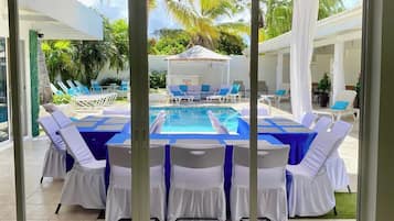 Uma área à beira da piscina com mesa e cadeiras, uma piscina e um espaço de estar coberto com guarda-sóis.