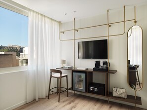 Quarto de hotel moderno com uma janela grande, uma escrivaninha com um laptop, uma cafeteira, um cofre e um espelho.