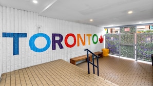 Paredes com a palavra "TORONTO" em letras coloridas, um banco de madeira, um contentor de lixo e uma porta de vidro que dá para o exterior.