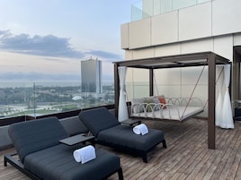 Um lounge no terraço com duas poltronas confortáveis, uma cama com dossel e vista para a cidade.