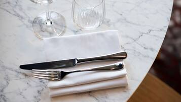Uma mesa posta com guardanapo branco, talheres e duas taças de vidro sobre uma superfície de mármore.