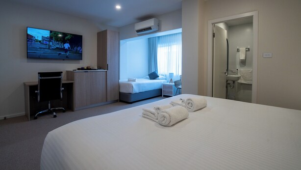 Quarto de hotel com uma cama grande, uma escrivaninha, uma cadeira, uma televisão, uma janela com cortinas, um banheiro e um ar-condicionado.