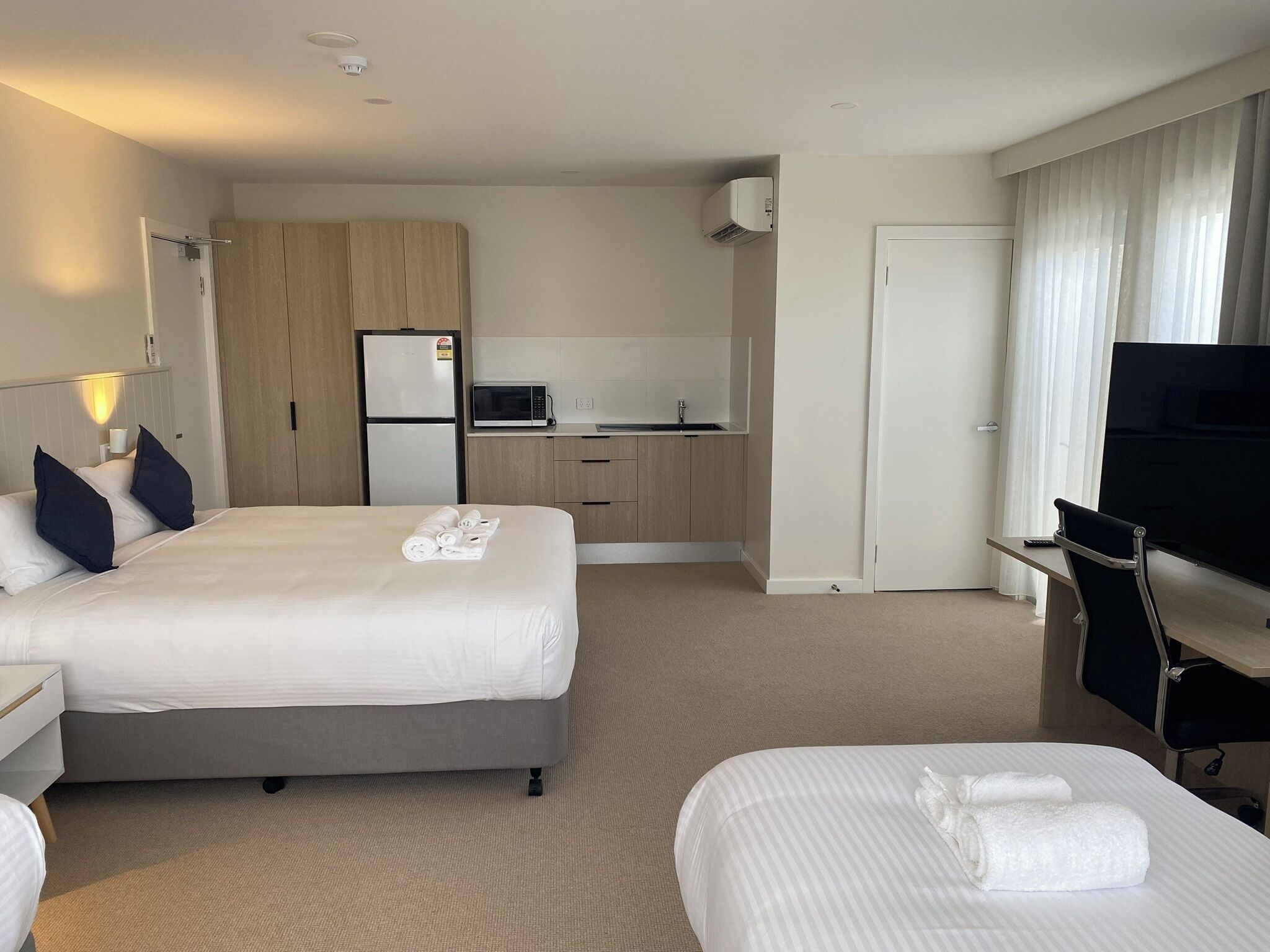Quarto de hotel com duas camas, uma cozinha compacta, uma televisão e uma mesa.
