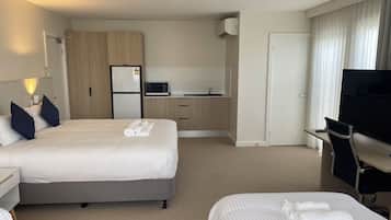 Quarto de hotel com duas camas, uma cozinha compacta, uma televisão e uma mesa.