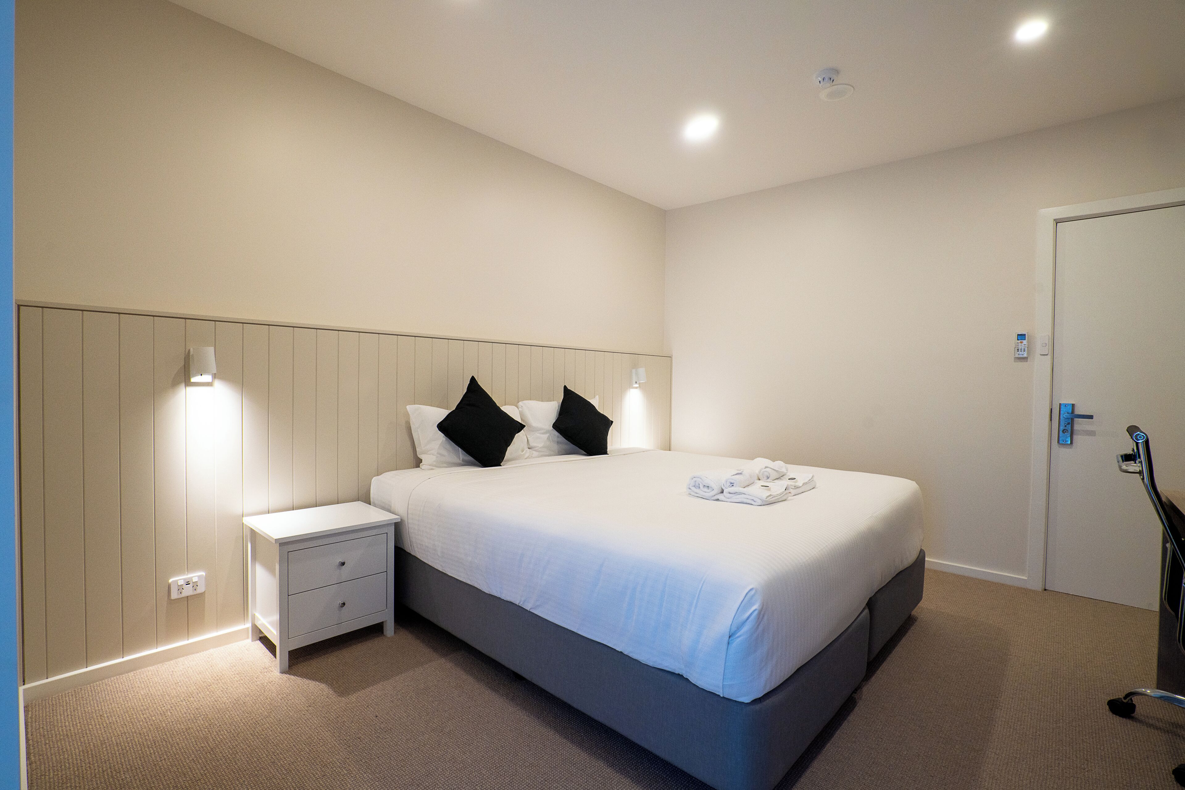 Quarto de hotel com cama, mesa de cabeceira e porta.
