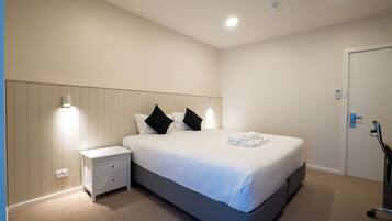 Quarto de hotel com cama, mesa de cabeceira e porta.