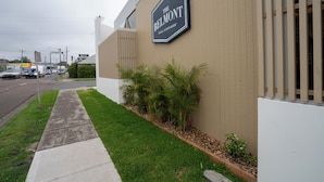Um edifício com uma placa que diz "The Belmont" e uma calçada com grama e pequenas plantas.