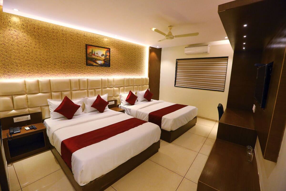 Quarto de hotel com duas camas, cabeceira, mesa de cabeceira com telefone e televisão na parede.