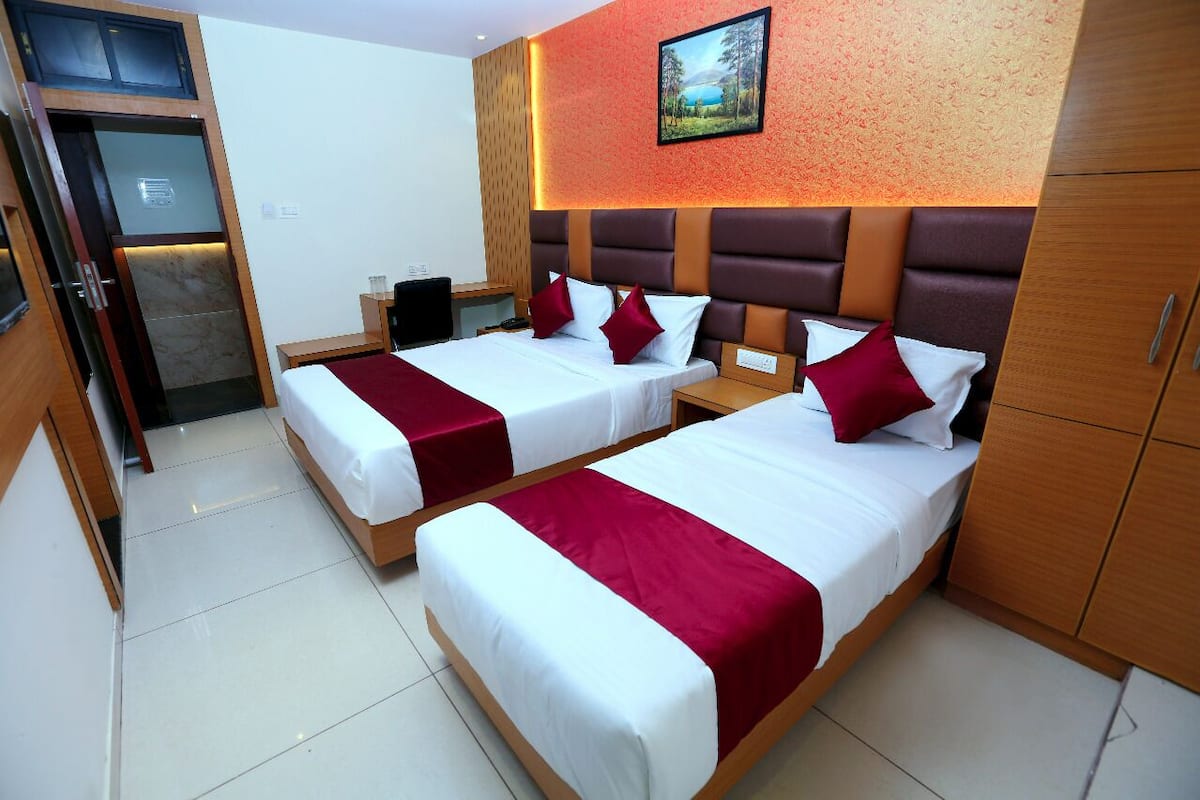 Quarto de hotel com duas camas, cada uma com roupa de cama branca e vermelha, cabeceira de madeira e mesa de cabeceira pequena.