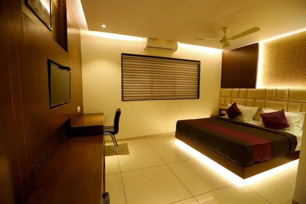 Um quarto com cama, escrivaninha, cadeira, ventoinha no teto e ar condicionado fixado na parede.