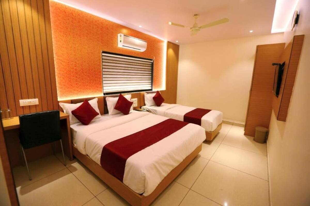 Quarto de hotel com duas camas, uma escrivaninha, uma cadeira, ar condicionado e ventoinha no teto.