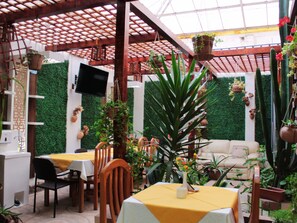 Um jardim interno com uma mesa e cadeiras, um sofá e diversos vasos de plantas.