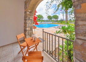 Uma varanda com vista para a piscina, paredes de pedra e mobiliário de madeira.