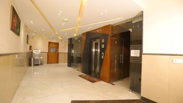 Um hall de hotel moderno com piso de mármore, balcão de recepção e elevador de vidro.