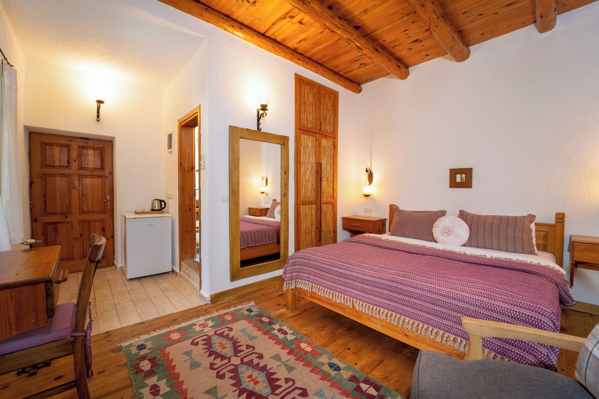 Quarto com cama, cabeceira de madeira, mesas de cabeceira, mesa de apoio, cômoda, escrivaninha e uma cadeira.