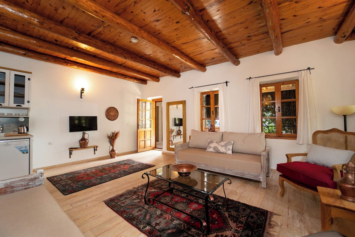 Uma sala de estar aconchegante com teto de madeira, um sofá, uma mesa de centro e uma televisão.
