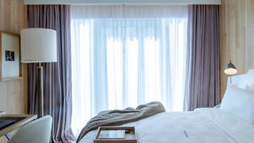 Quarto de hotel com cama, escrivaninha, luminária e janela com cortinas.