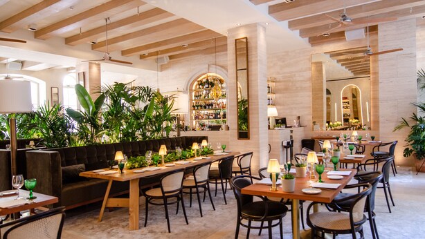 Restaurante com mesas e cadeiras de madeira, área de bar e um espelho grande.