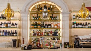Uma área de bar com prateleiras cheias de garrafas de bebidas, uma máquina de café e um caixa registradora.