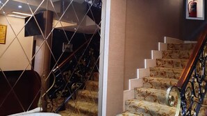 Uma escadaria com carpete estampado e guarda-mão de metal, conduzindo a uma área escura.