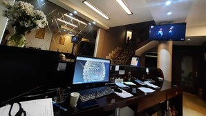 Uma receção de hotel com vários monitores de computador, um telefone e um vaso de flores.