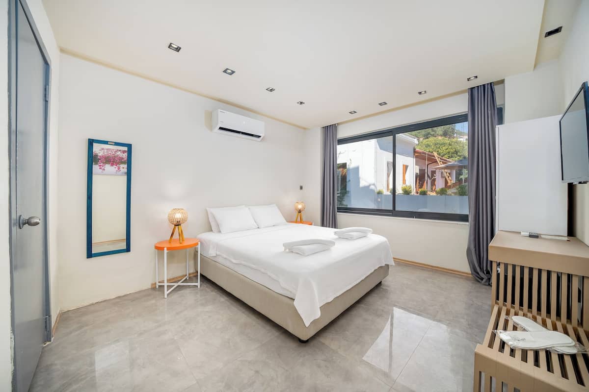 Quarto de hotel moderno com uma cama grande, uma mesa de cabeceira com luminária, televisão e berço.