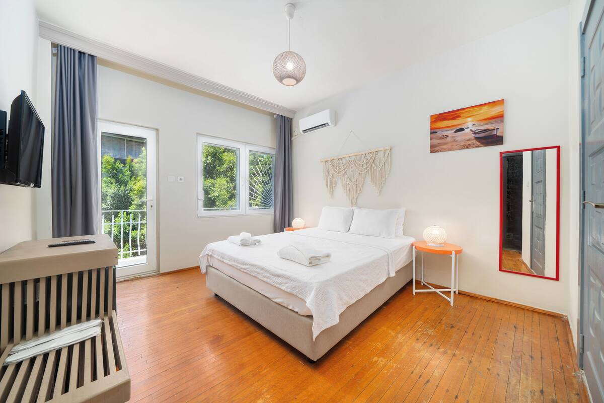 Quarto com uma cama grande, televisão, janela com cortinas, luminária no teto e obras de arte nas paredes.