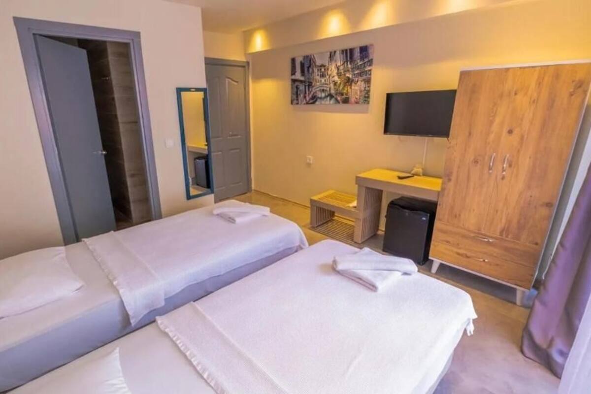 Quarto de hotel com duas camas, uma escrivaninha com cadeira, um guarda-roupa, uma televisão e uma porta que dá para um armário.