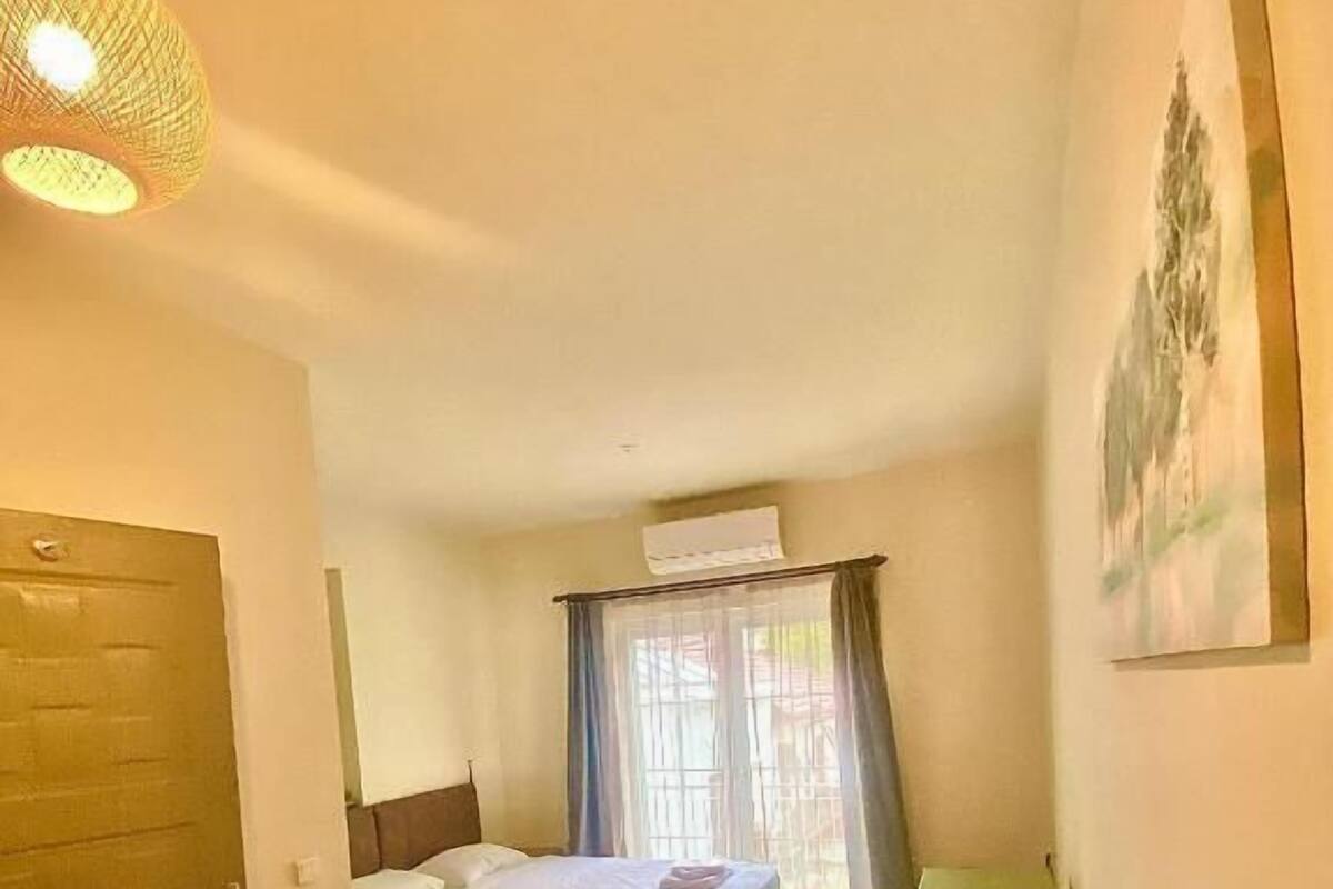Quarto com cama, escrivaninha e janela com cortinas.