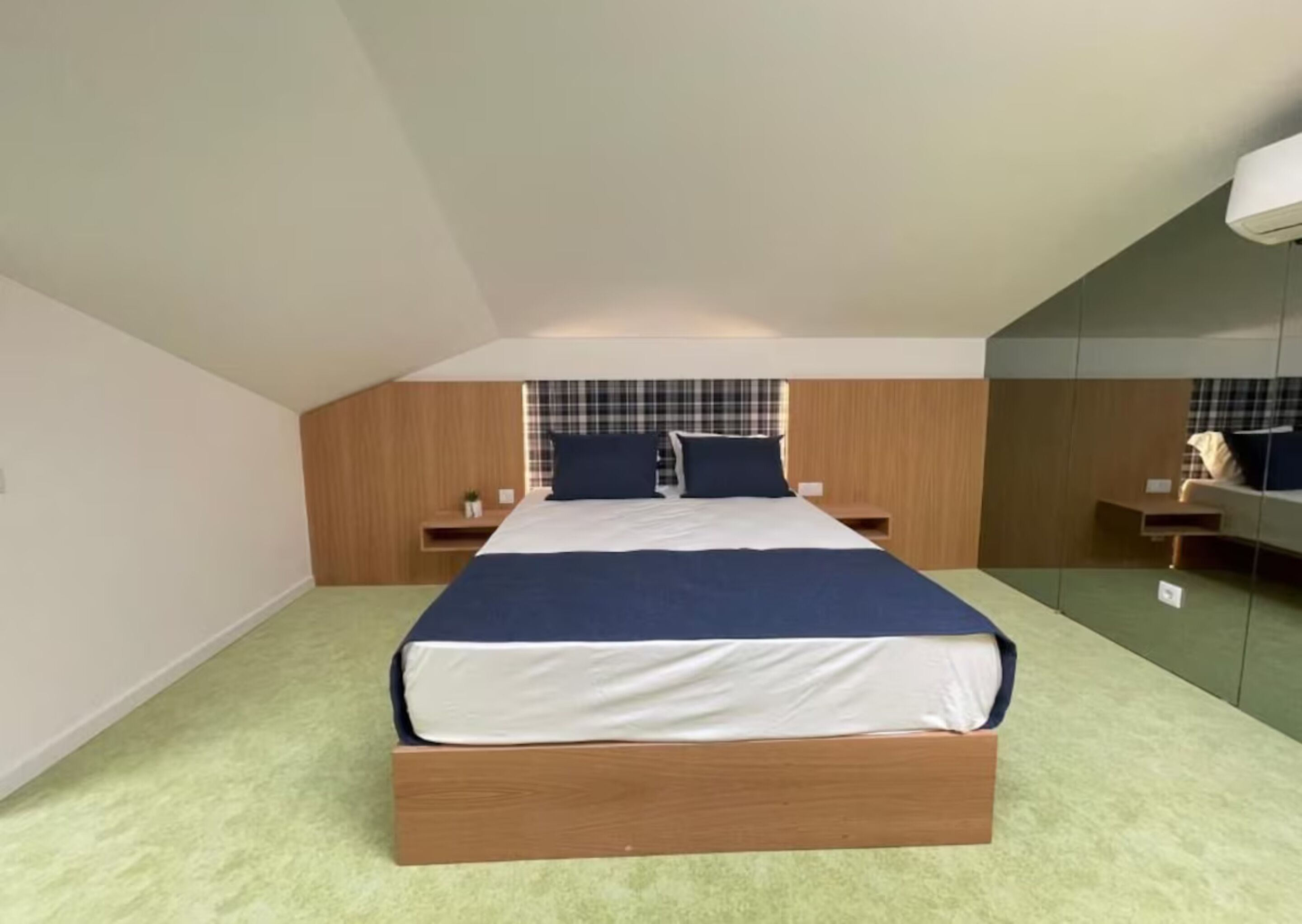 Quarto moderno com cama grande, cabeceira de madeira e tapete verde.