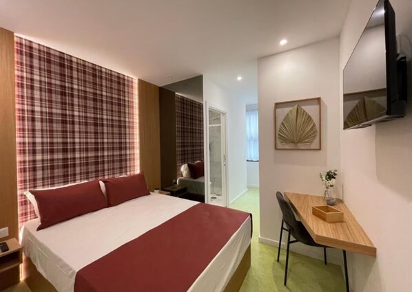 Quarto de hotel com uma cama grande, uma escrivaninha e uma televisão.