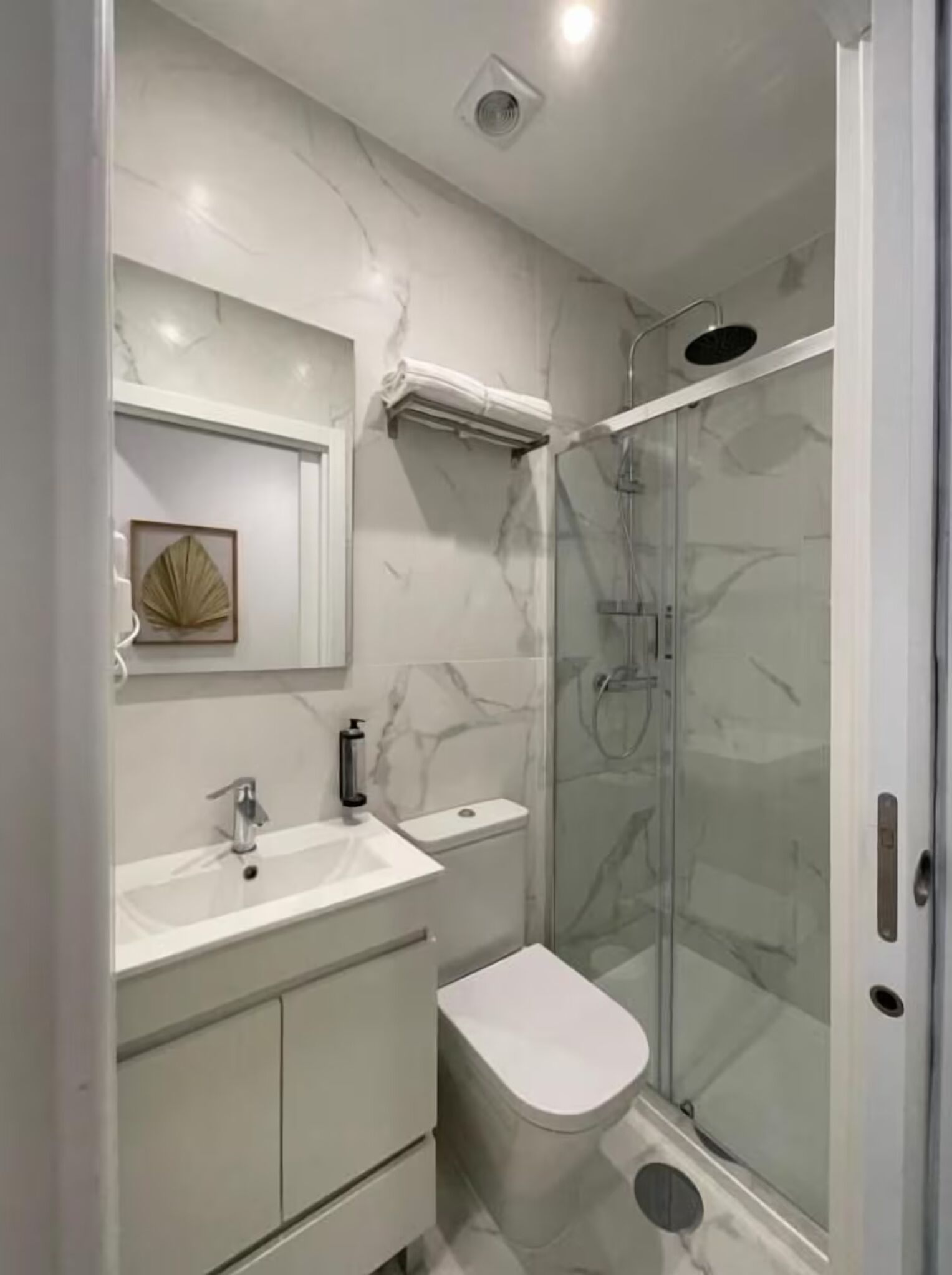 Uma casa de banho moderna com lavatório de mármore, sanita e cabine de duche envidraçada.