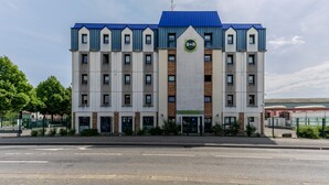 Um hotel com vários andares e telhado azul, com uma placa central que diz "B&B Hotels".