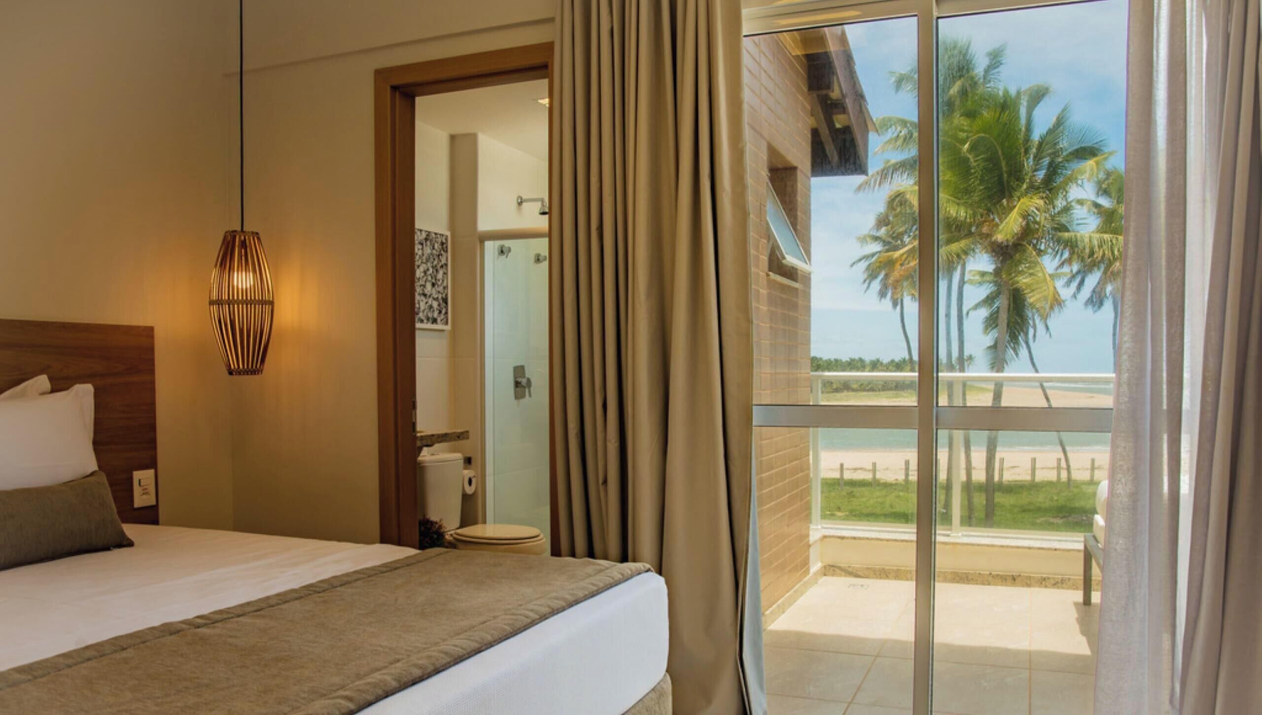 Quarto de hotel com cama, chuveiro e varanda com vista para palmeiras.