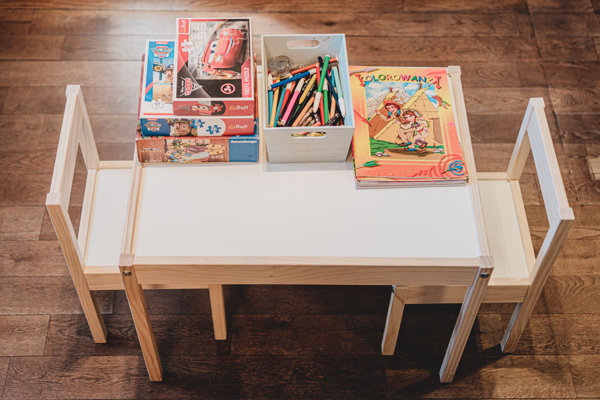 Uma mesa de madeira com tampo branco, cercada por diversos brinquedos e livros infantis.