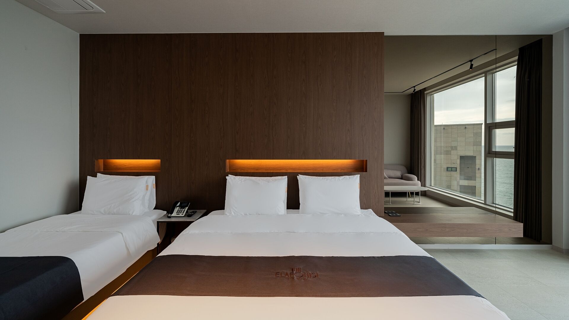 Quarto de hotel com duas camas, vista da cidade e uma janela grande.