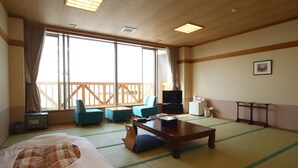 Um quarto em estilo japonês tradicional, com tatames, uma mesa de madeira baixa, um sofá e uma televisão.