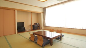 Um quarto japonês tradicional com soalho de esteiras de tatami, uma mesa de madeira, quatro bancos de tatami, uma televisão e uma porta deslizante.