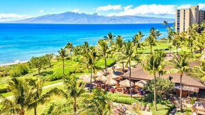 Um resort com vista para o oceano e montanhas, com palmeiras, área de estar ao ar livre e um edifício com vários andares.