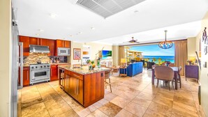 Uma cozinha ampla com ilha central, sala de jantar com vista para o oceano e sala de estar com grande janela para o mar.