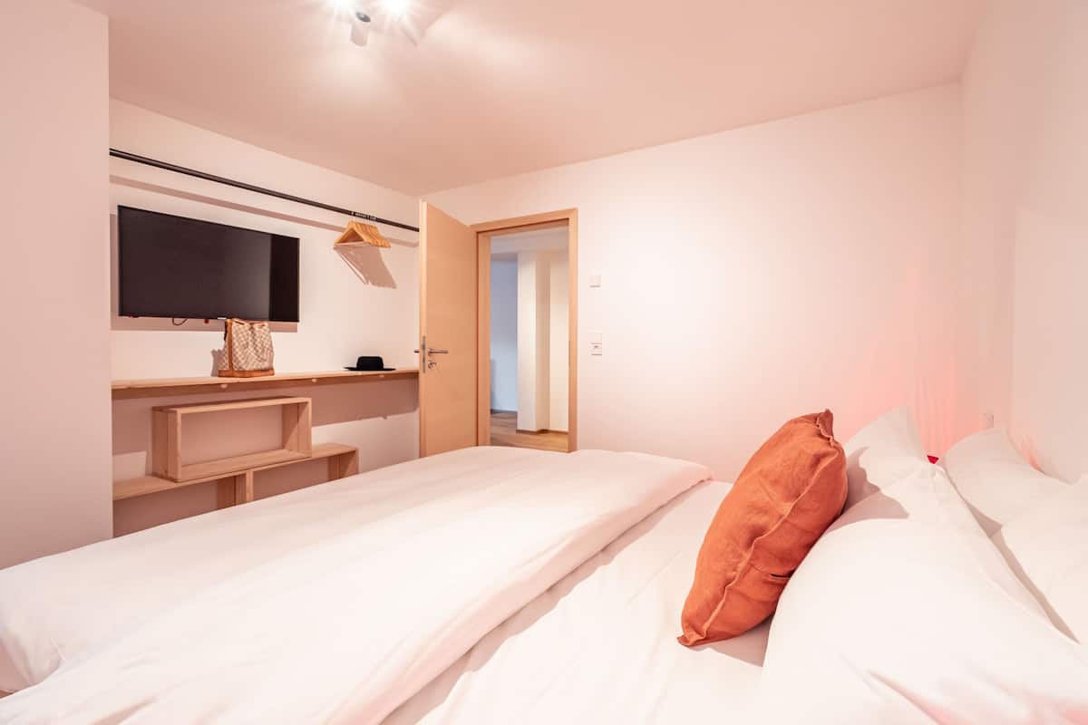 Quarto de hotel moderno com cama, televisão na parede e escrivaninha de madeira.