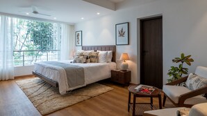 Um quarto moderno com uma cama grande, mesas de cabeceira, um criado-mudo, uma luminária de leitura, uma mesa de centro e uma cadeira.