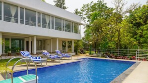 Um edifício moderno com piscina, cadeiras de descanso listradas em azul e branco, e um jardim bem cuidado.