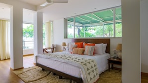 Quarto espaçoso com cama grande, cabeceira de madeira e vista para um telhado verde.