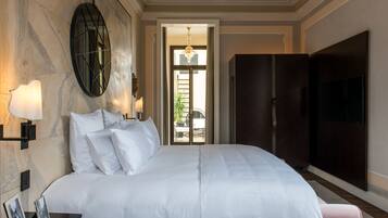 Quarto de hotel com cama grande, televisão na parede, espelho e porta para uma varanda.