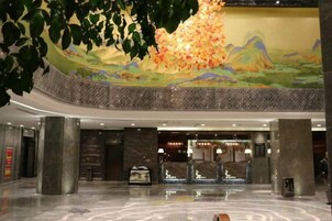 Um saguão de hotel com uma recepção, um grande mural e piso de mármore.