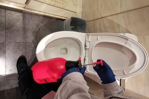 Uma pessoa limpando um vaso sanitário com uma ferramenta de limpeza vermelha.