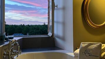 Casa de banho com banheira, janela com vista para o céu e um espelho redondo na parede.